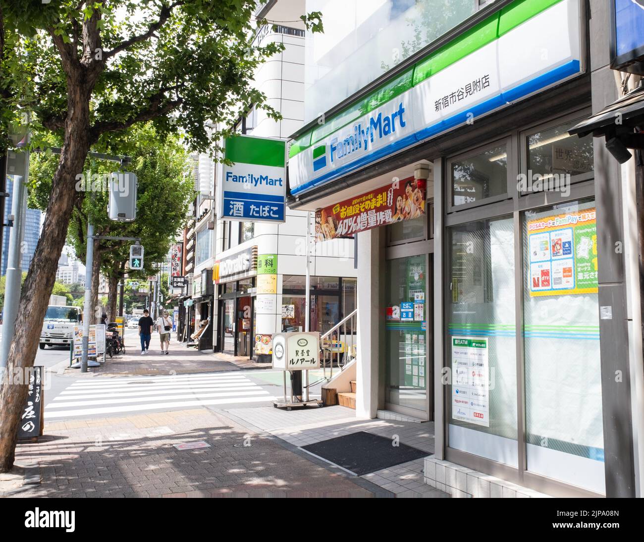 The storefront shot from a busy shaded sidewalk of a FamilyMart, a ...