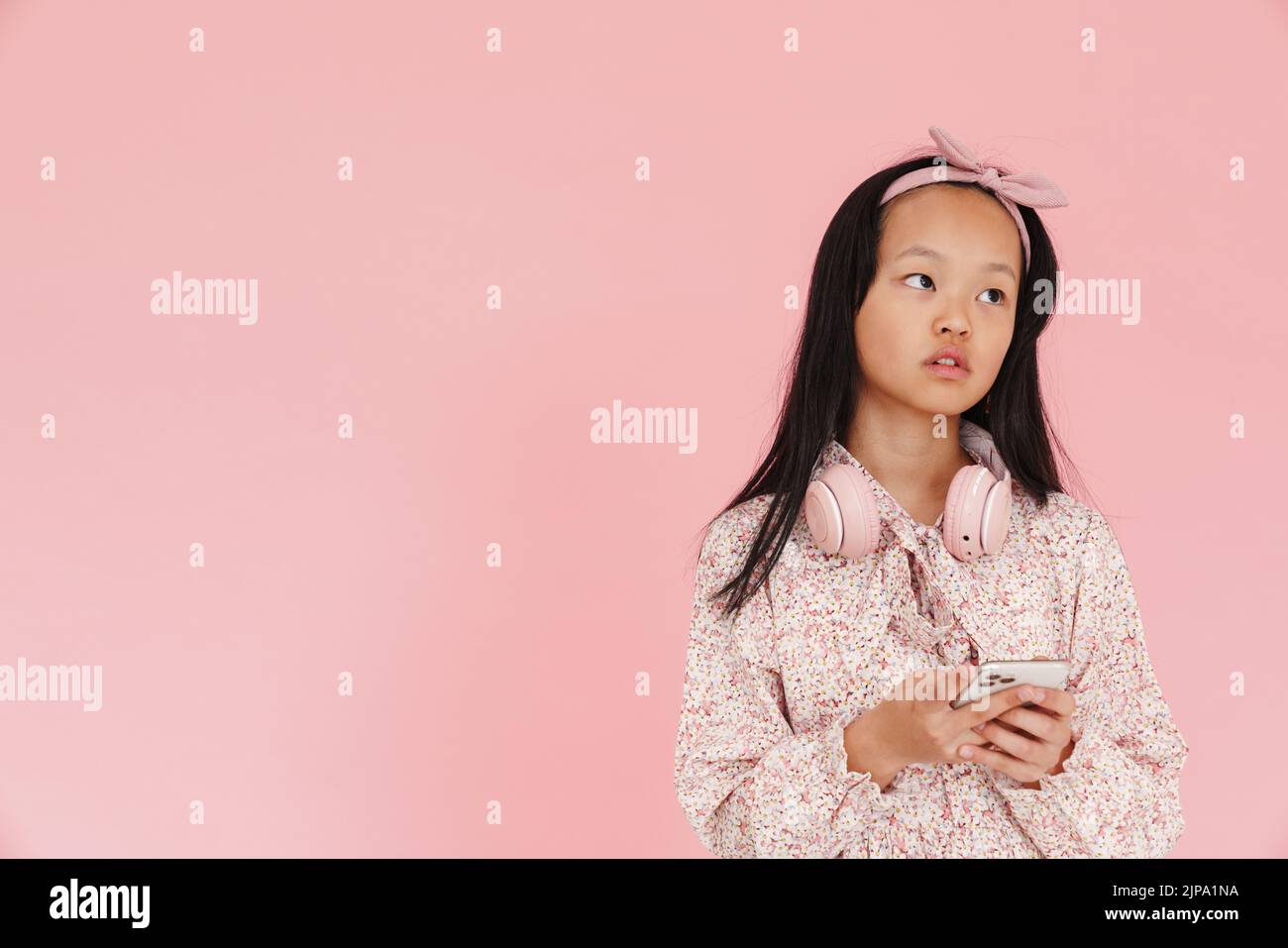 Asian puzzled girl with headphones using mobile phone isolated over ...