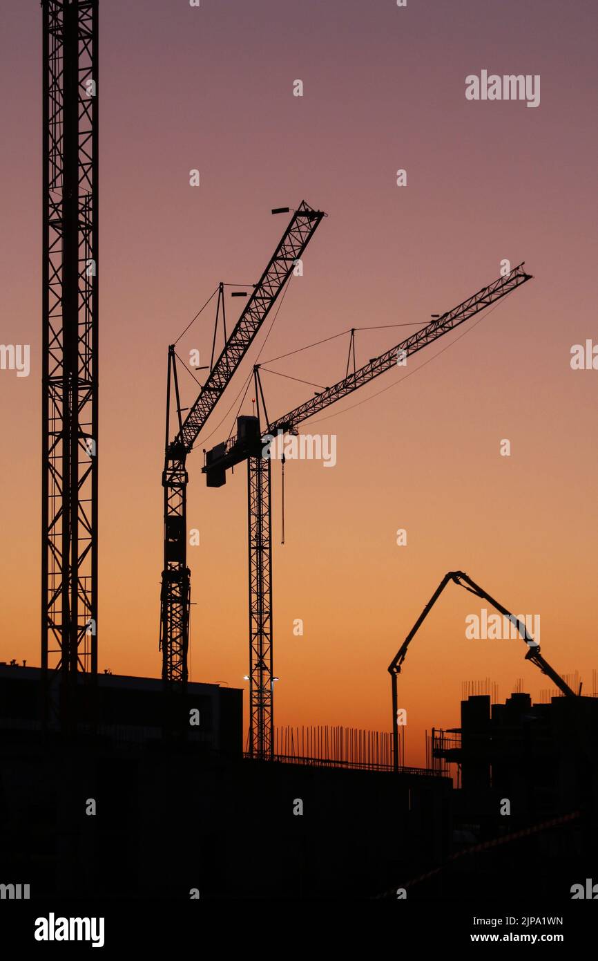 Construction cranes seen against the backdrop of the setting sun ...
