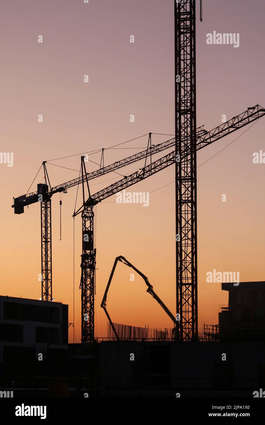 Construction cranes seen against the backdrop of the setting sun ...