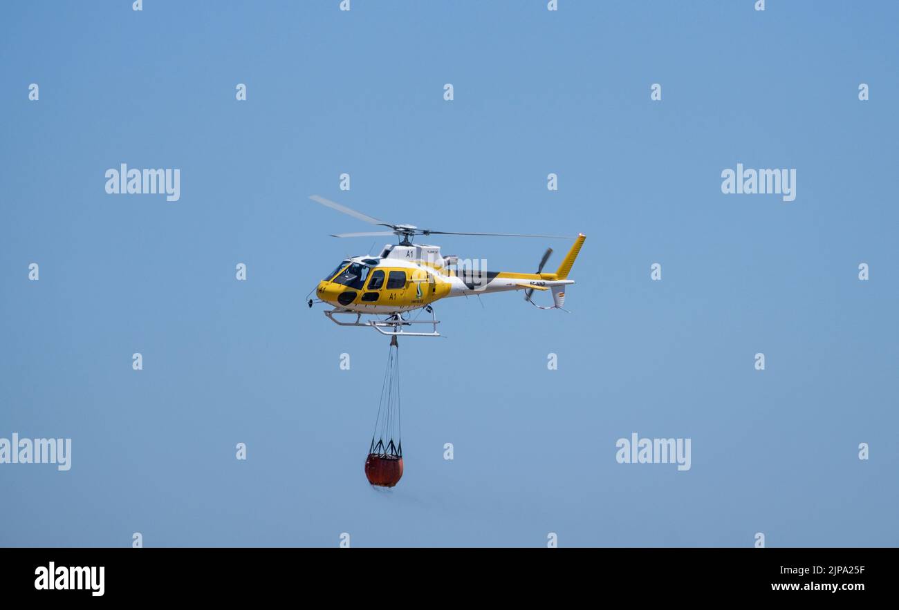 A firefighting service helicopter carrying a basket with water flying ...