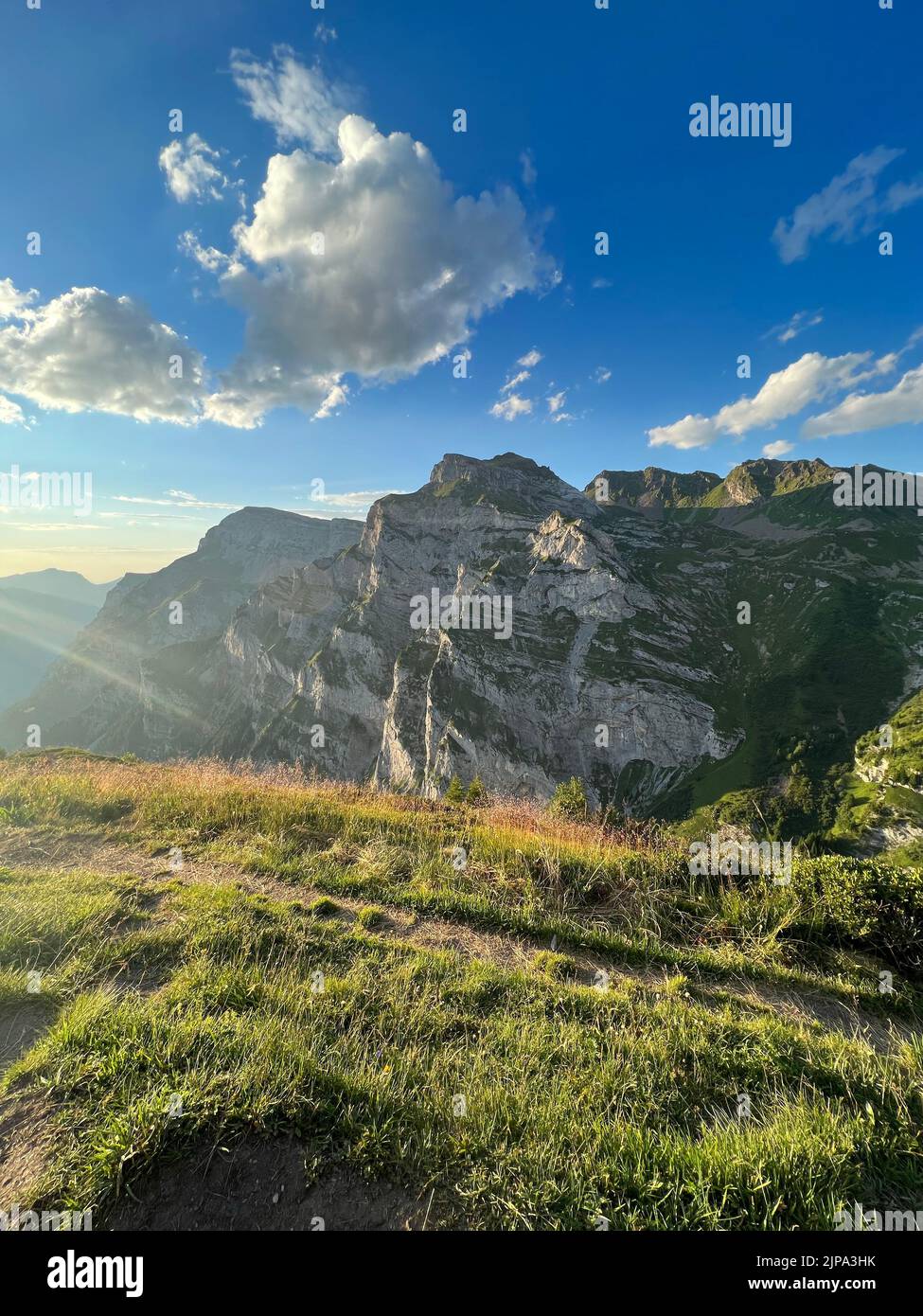 A landscape with green grass under sunlight and rocky mountains under ...