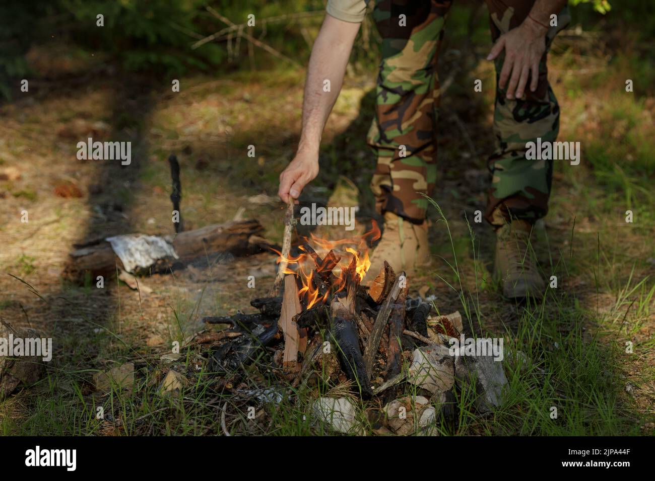 Man in military clothes is making campfire in the woods. The concept of ...