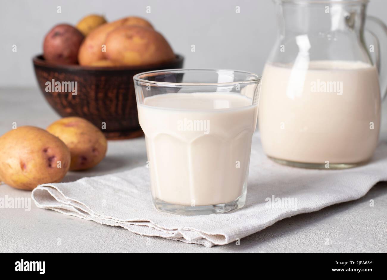 Vegan potato milk in glass and in jug on light gray table. Use of plant ...