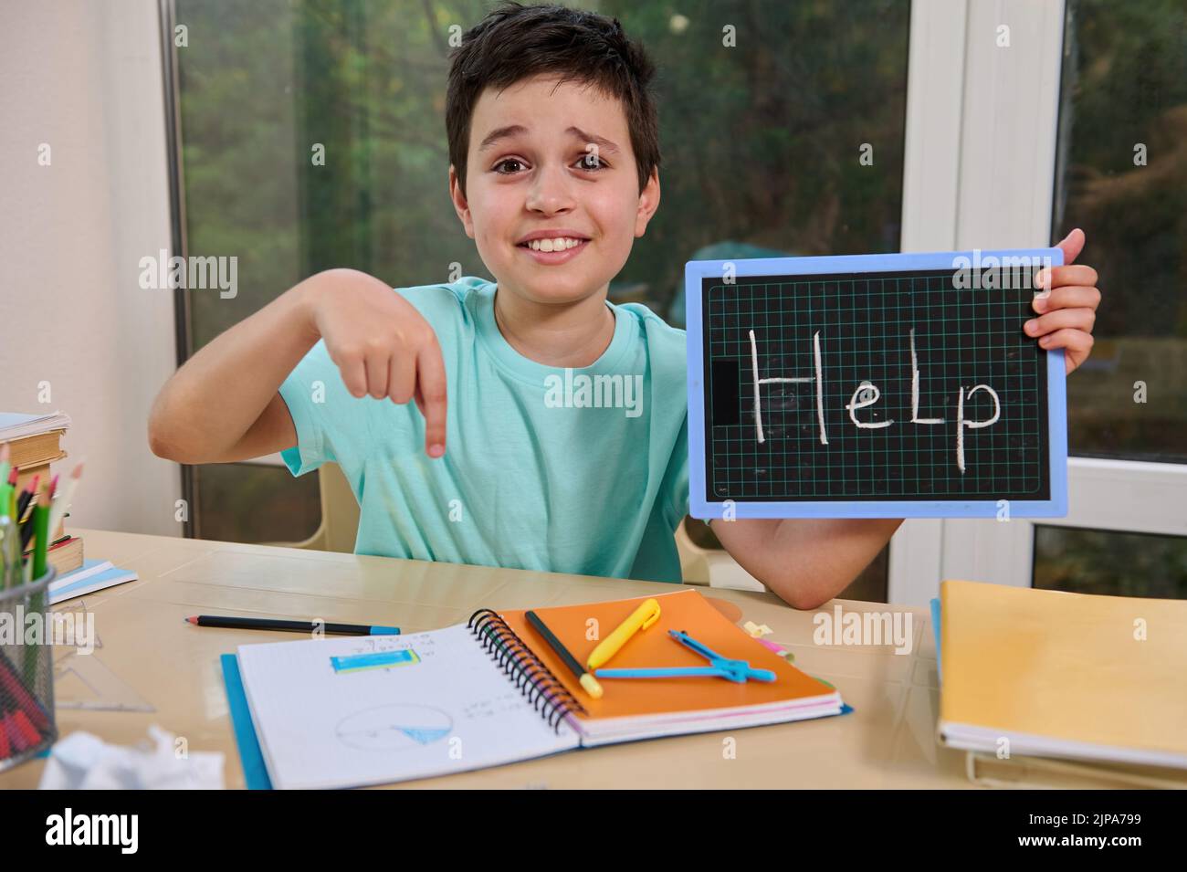 Puzzled schoolboy holds a blackboard HELP, points his finger at a ...