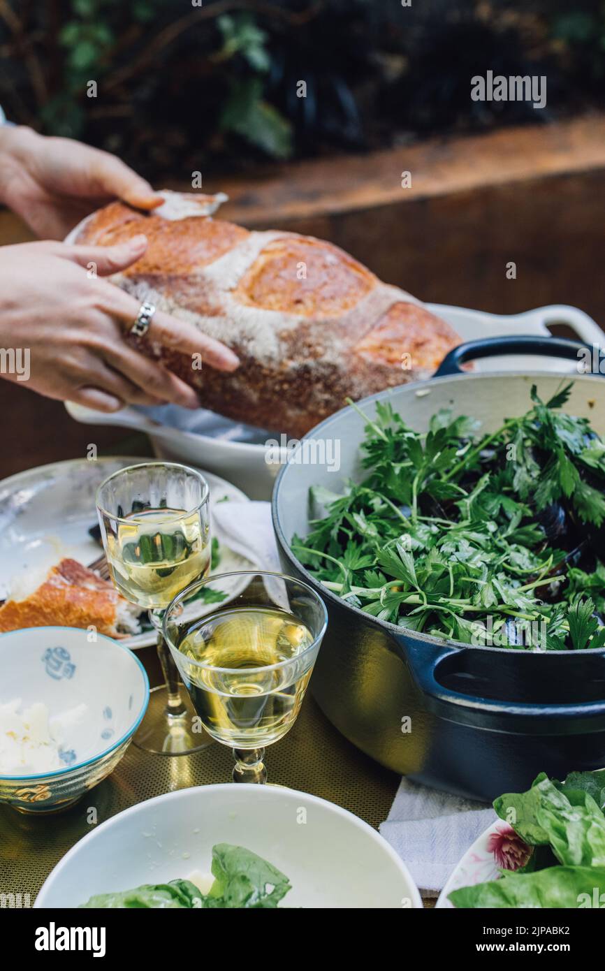 woman breaking bread at summer evening dinner table with salad, white ...