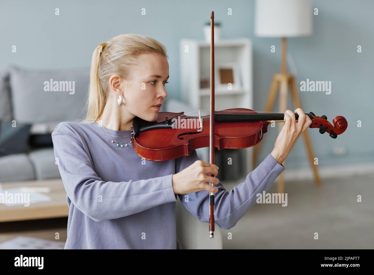 Side view portrait of elegant blonde woman playing violin at home or in ...