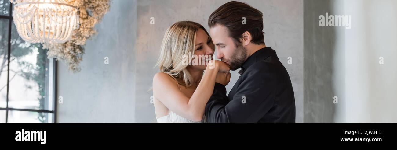 Bearded man in suit kissing hand of smiling girlfriend in restaurant ...