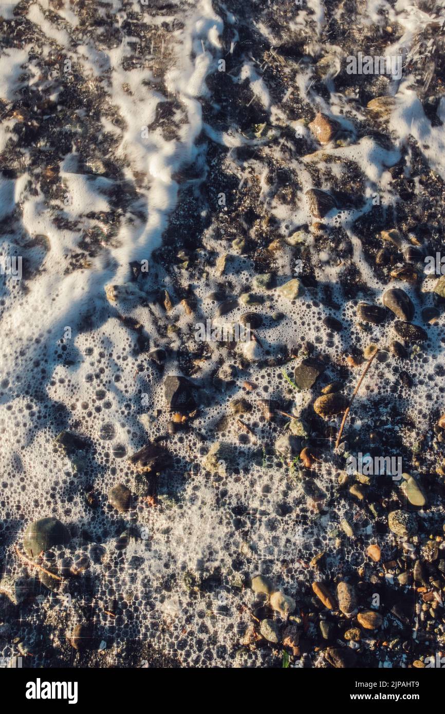foaming, sparkling water waves on rocky beach Stock Photo - Alamy