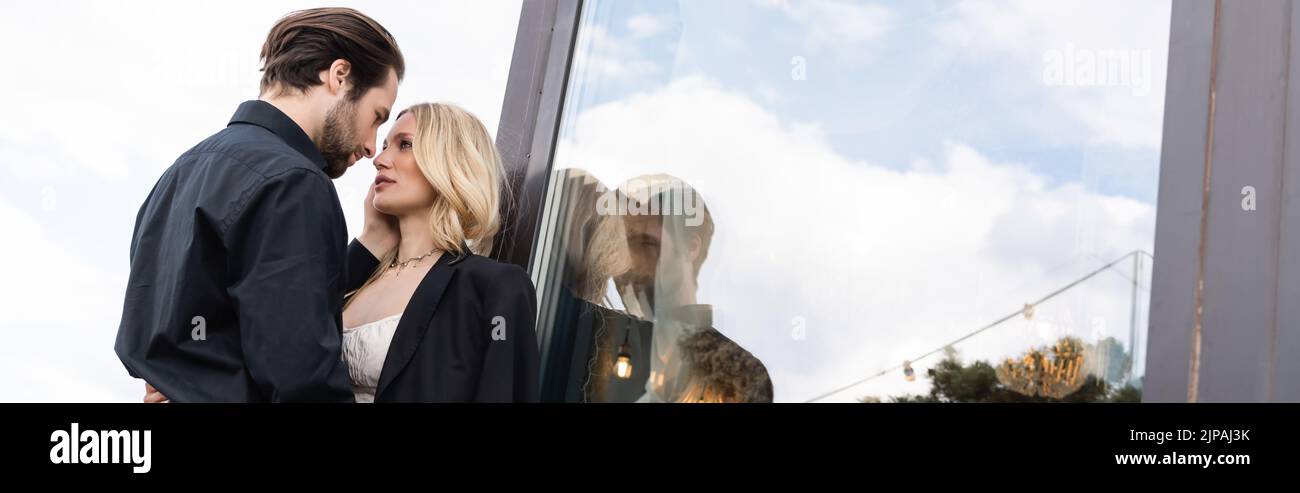 Low angle view of brunette man kissing girlfriend in jacket on terrace ...