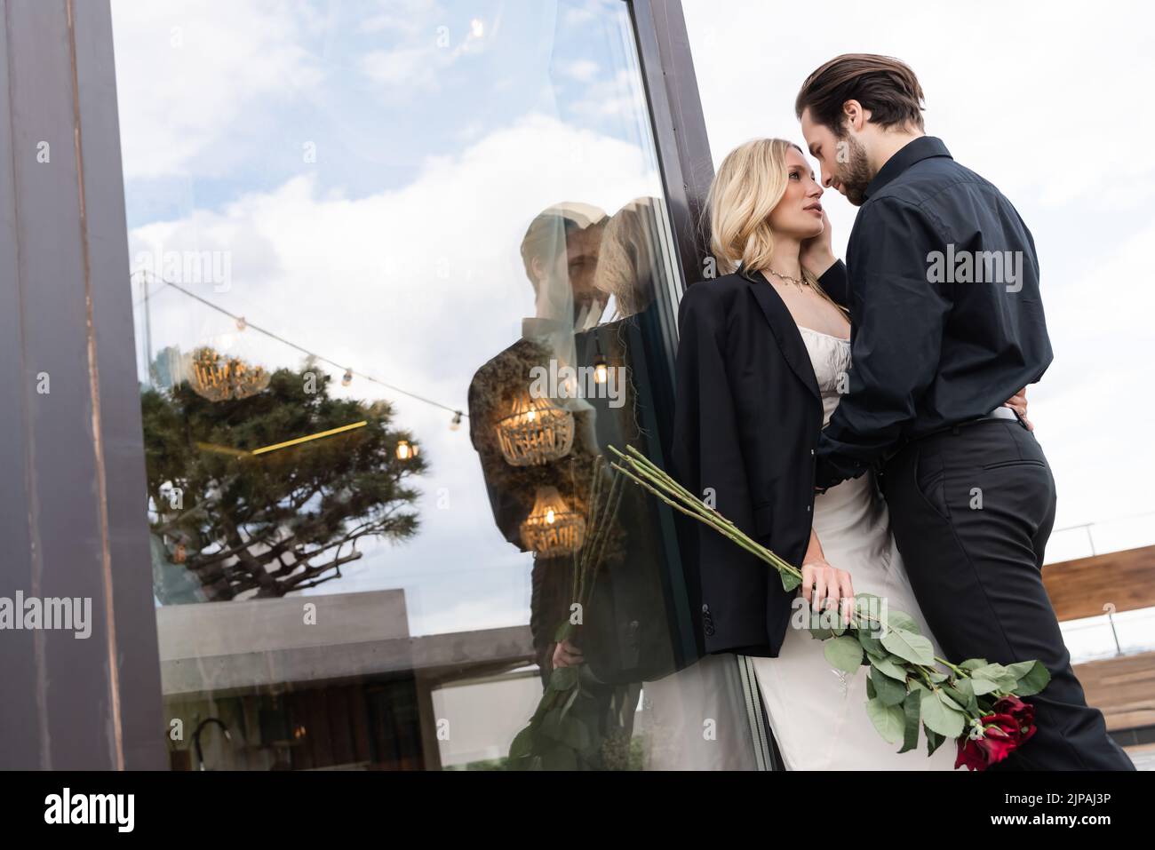 Low angle view of man kissing girlfriend with red roses on terrace of ...