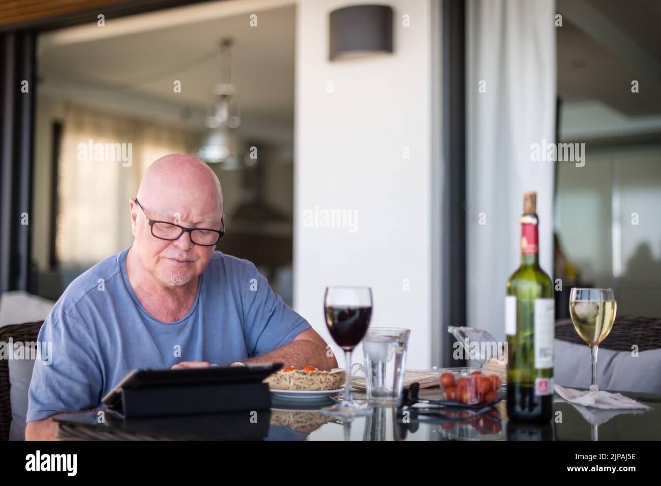An old caucasian man having dinner while working on his tablet Stock ...