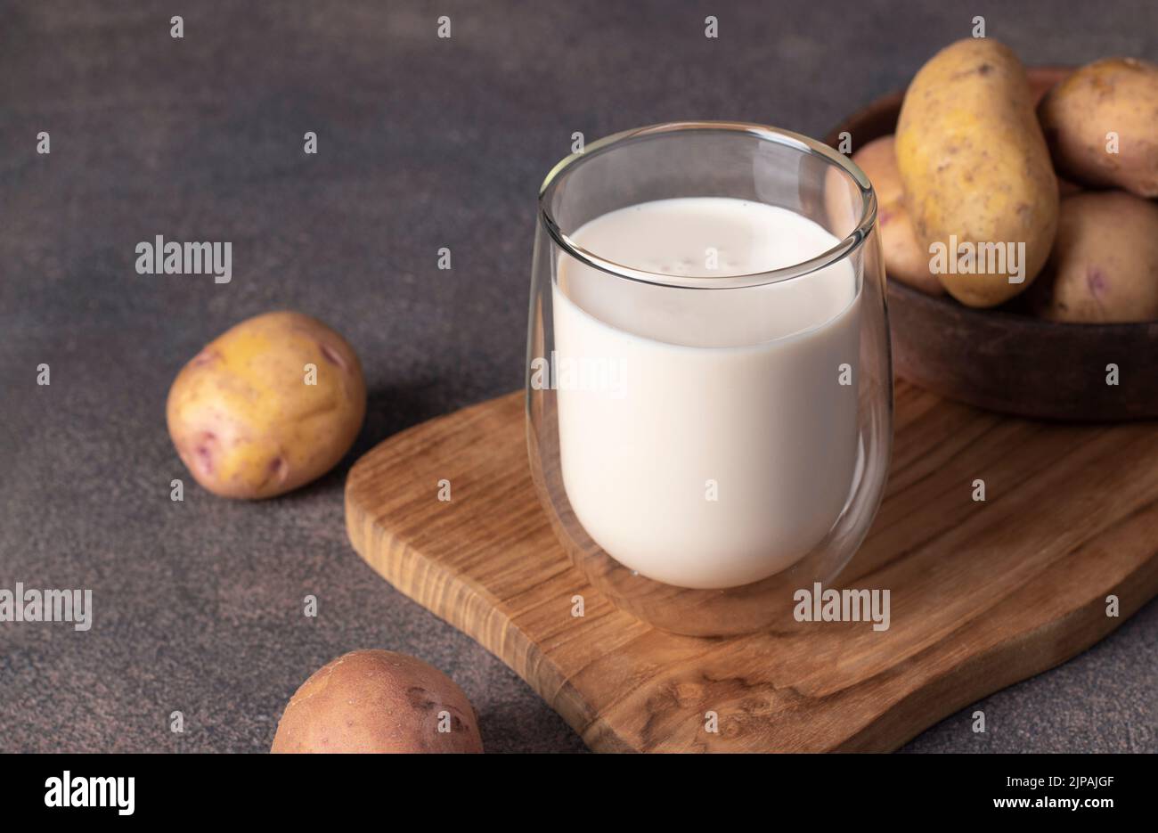 Vegan potato milk in glass and potato in plate on wooden board. Plant ...