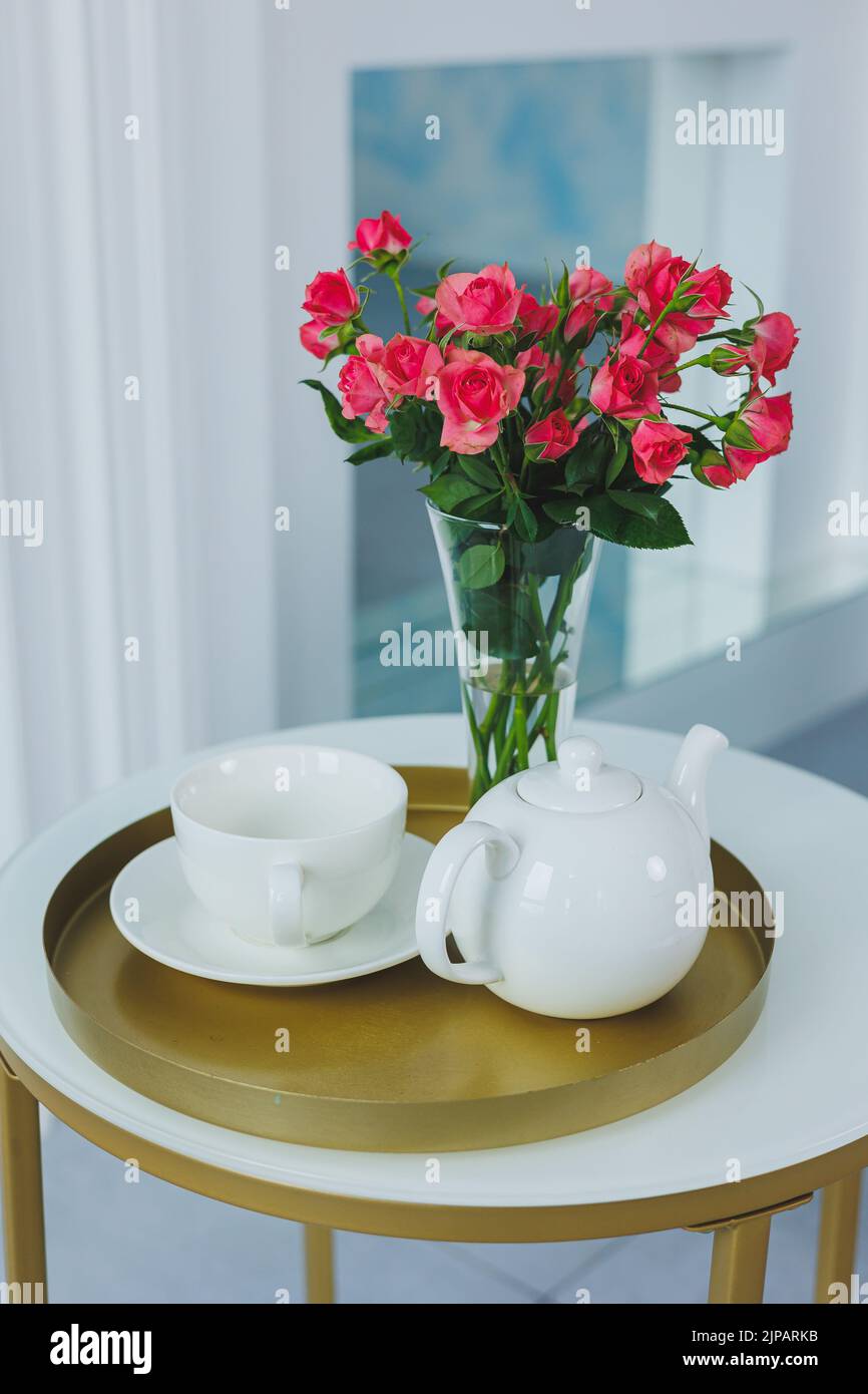 A table with a white teapot and a white cup. on the table a vase with ...