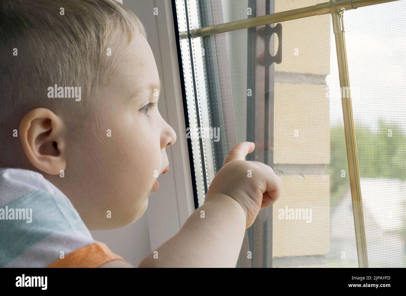 A little boy sits and looks out the window, points his finger. Close-up ...
