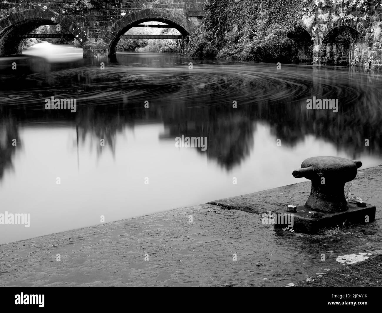 A grayscale of a reflective river in a park with a stone bridge Stock ...