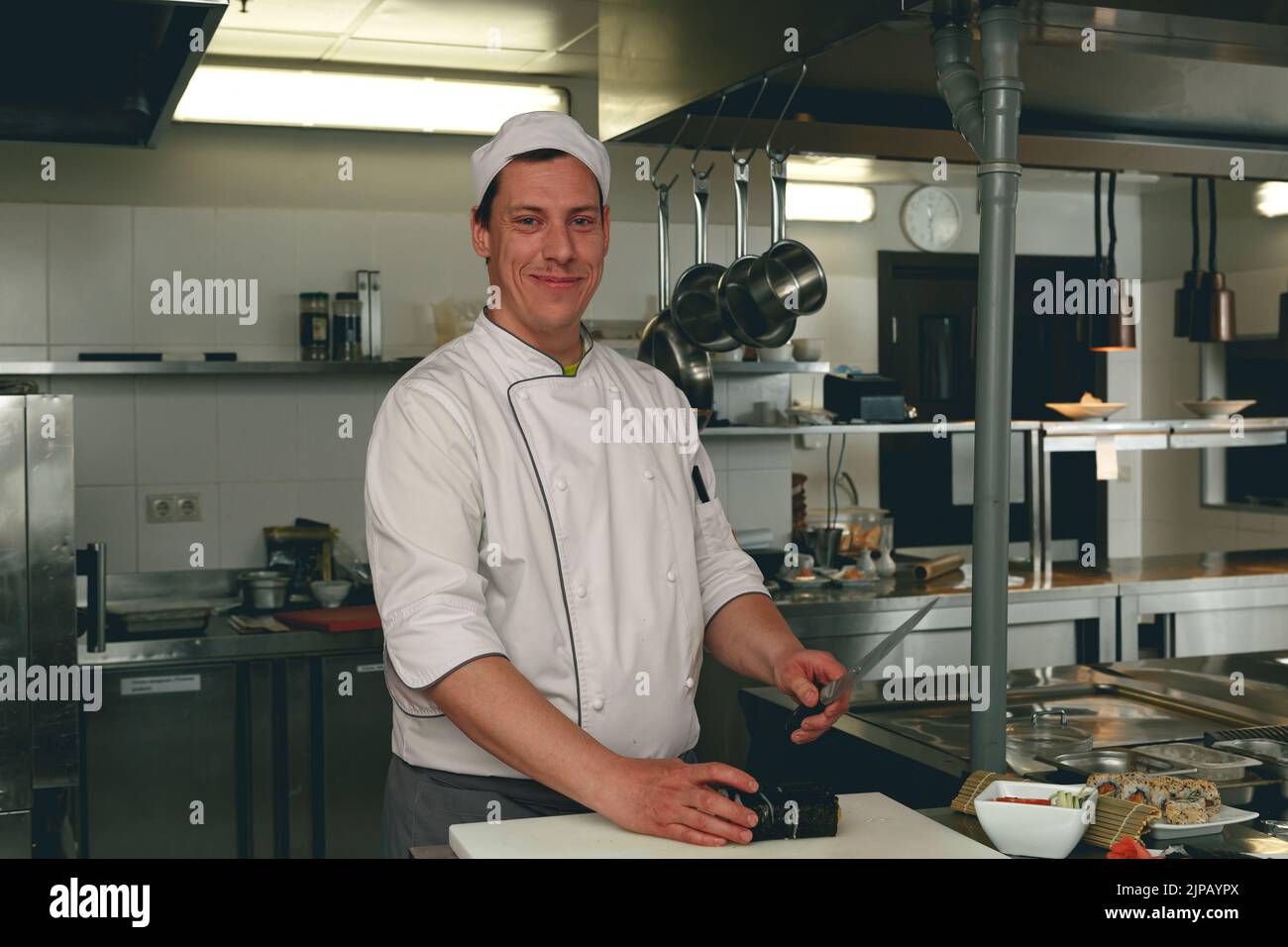 Smiling Male Chef in uniforms preparing sushi in a kitchen of asian ...