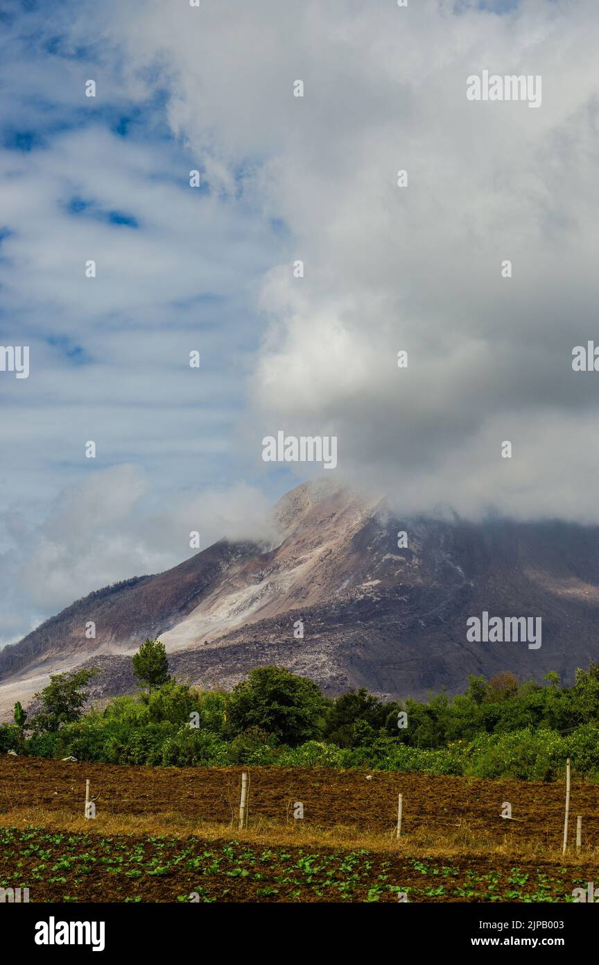 A vertical shot of the Merapi volcano peak covered in a white cloud ...