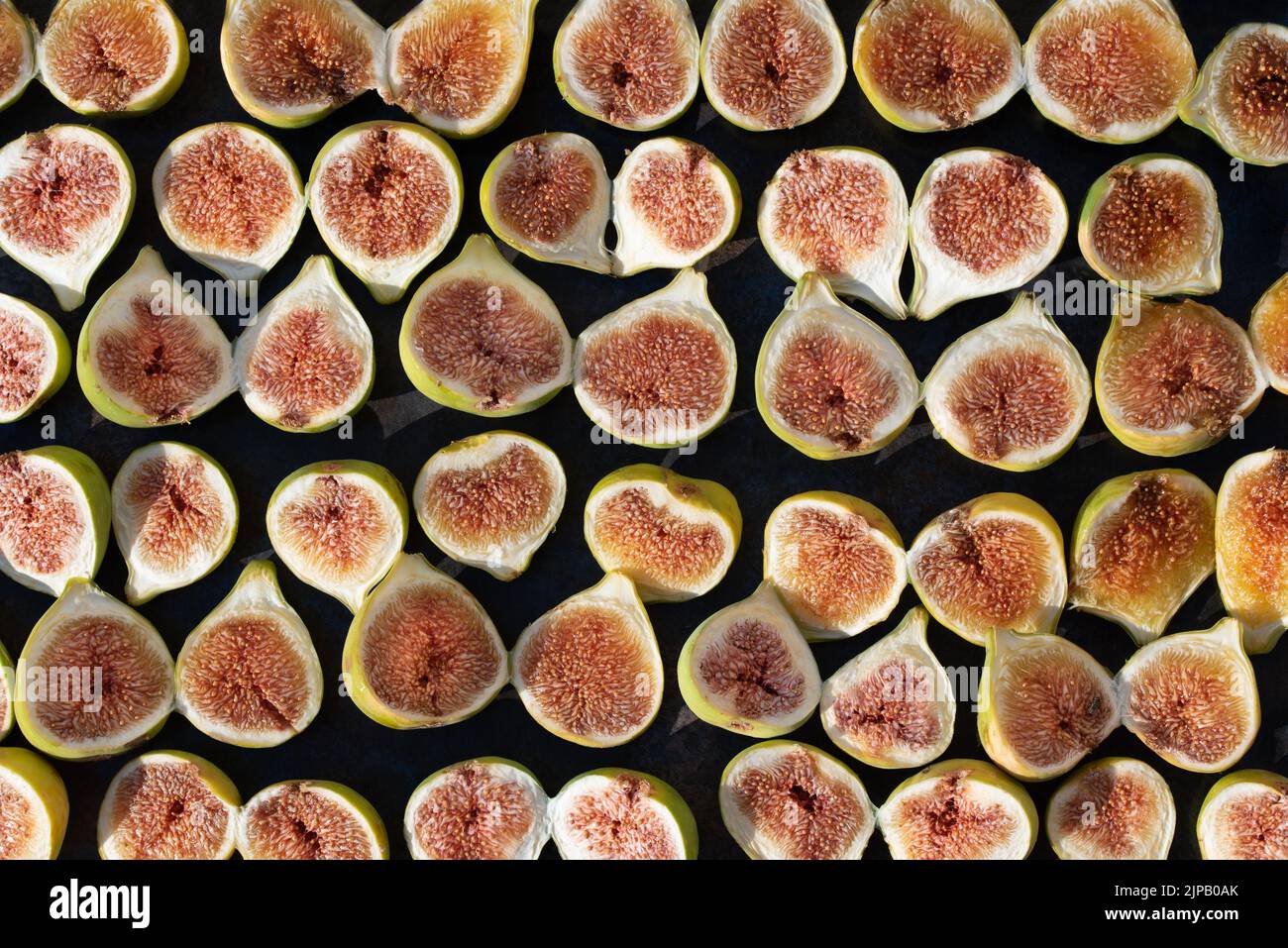 Many green, freshly cut figs lie next to each other in front of a dark ...