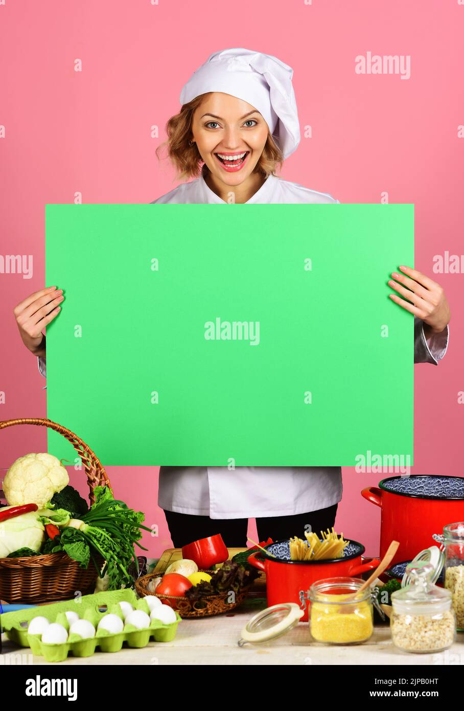 Beautiful smiling female chef in uniform and hat with advertising board ...