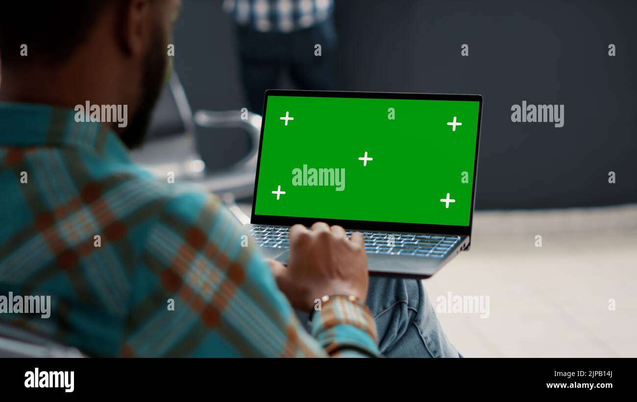 Male patient using greenscreen display on laptop computer, sitting in ...