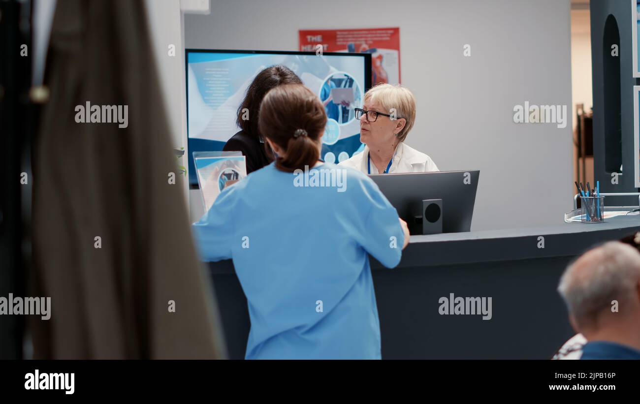 Medical staff and secretary talking at hospital reception desk, working on administrative ...