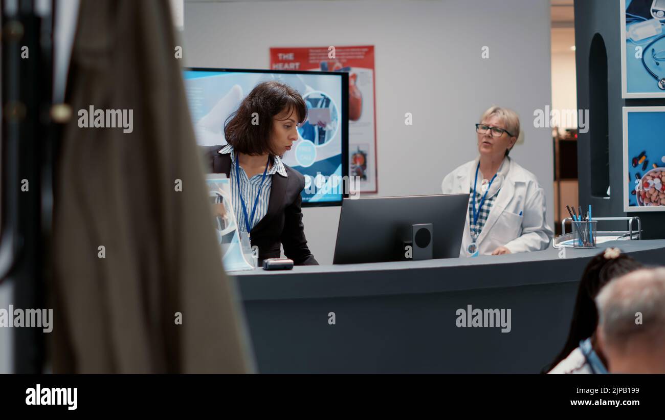 Hospital employee working on appointment service at reception desk, giving administrative ...