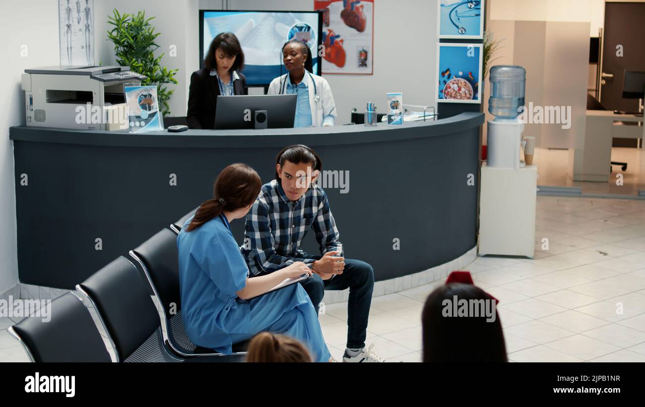 Medical assistant chatting with asian man and taking notes on checkup ...