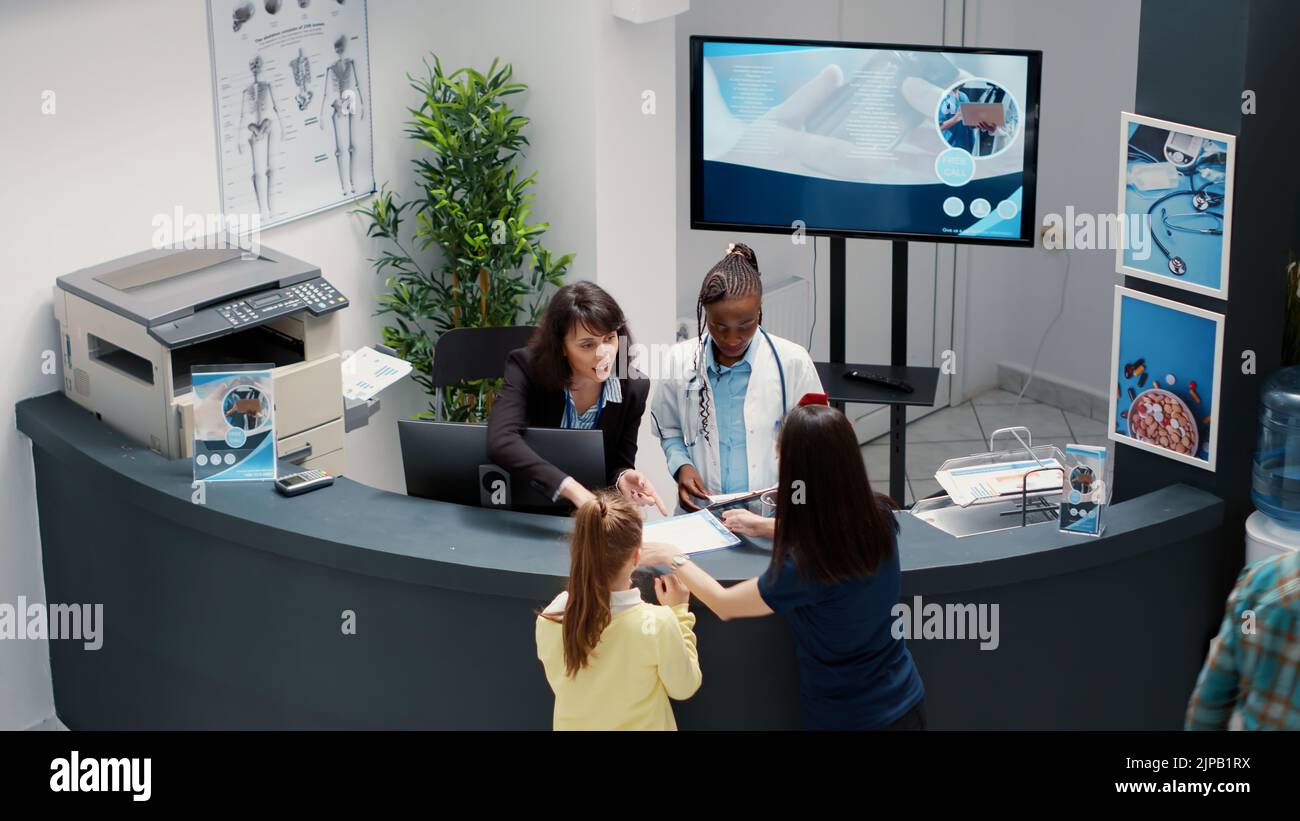 Secretary working at busy hospital reception desk to help patients with ...