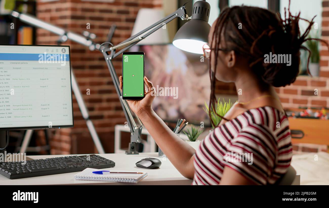 Female employee holding smartphone with greenscreen display at home ...