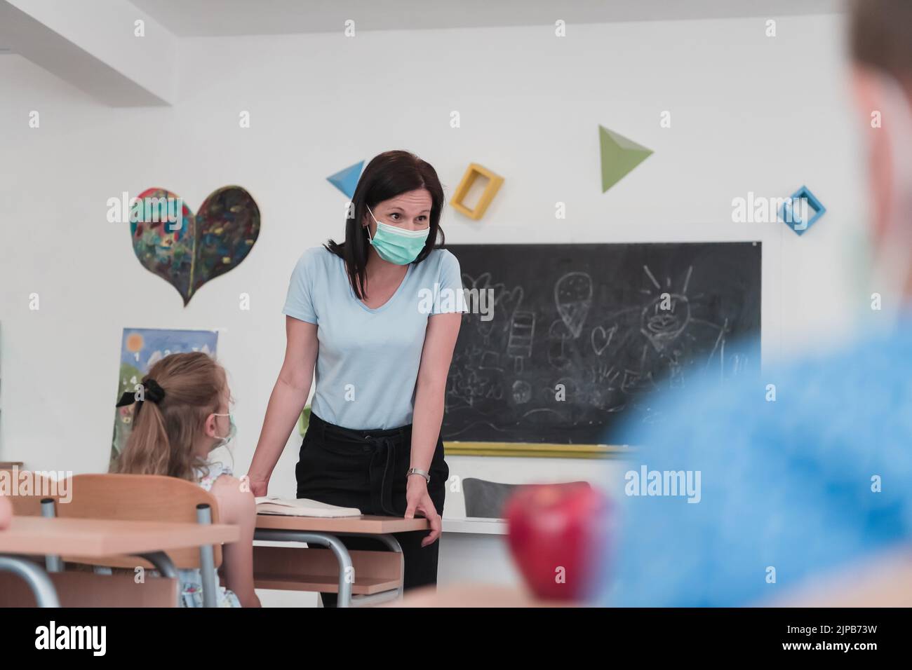 Multiracial group of kids wearing face masks working at class, writing ...
