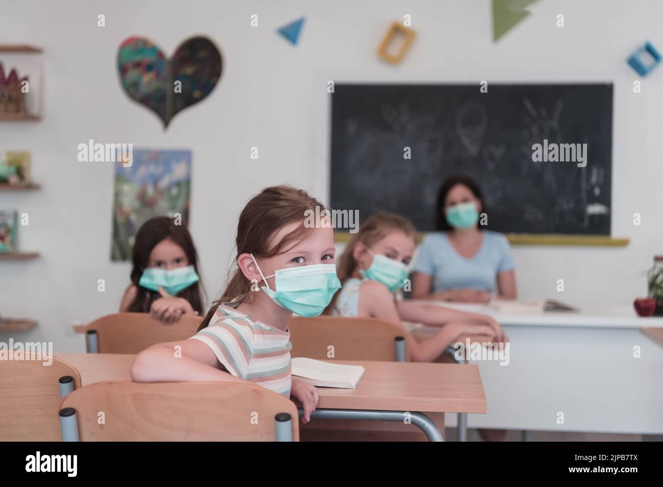 Multiracial group of kids wearing face masks working at class, writing ...