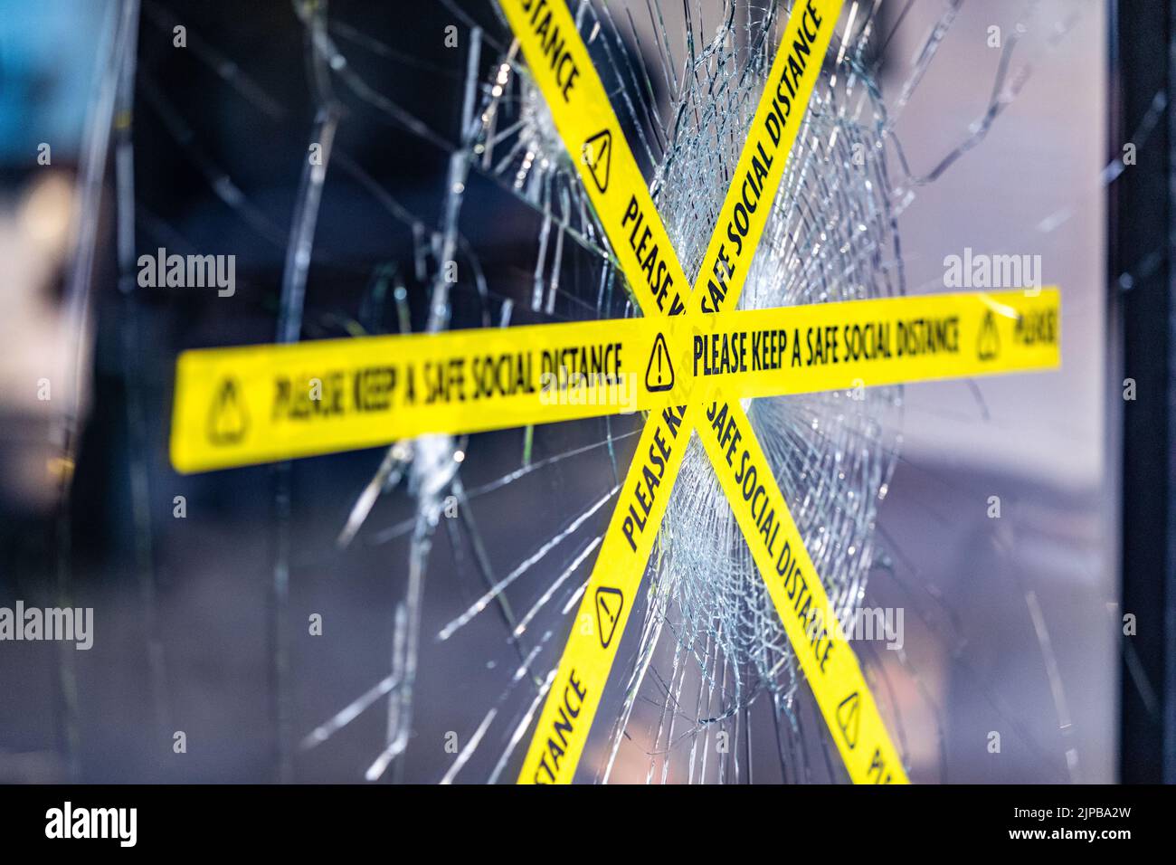 A closeup of a cracked window with yellow safety tapes warning about ...