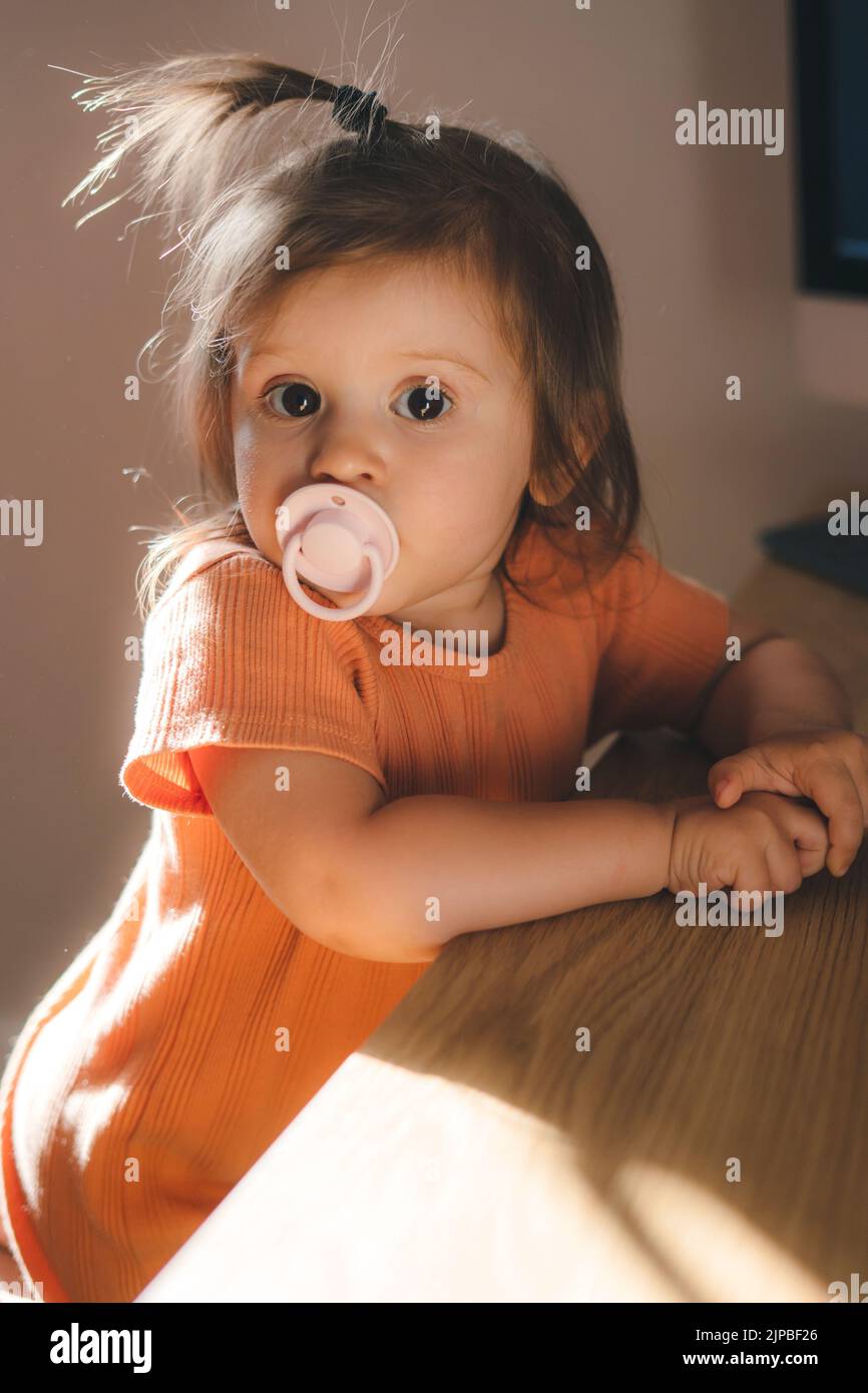 Portrait of adorable baby girl with pacifier in mouth looking very ...