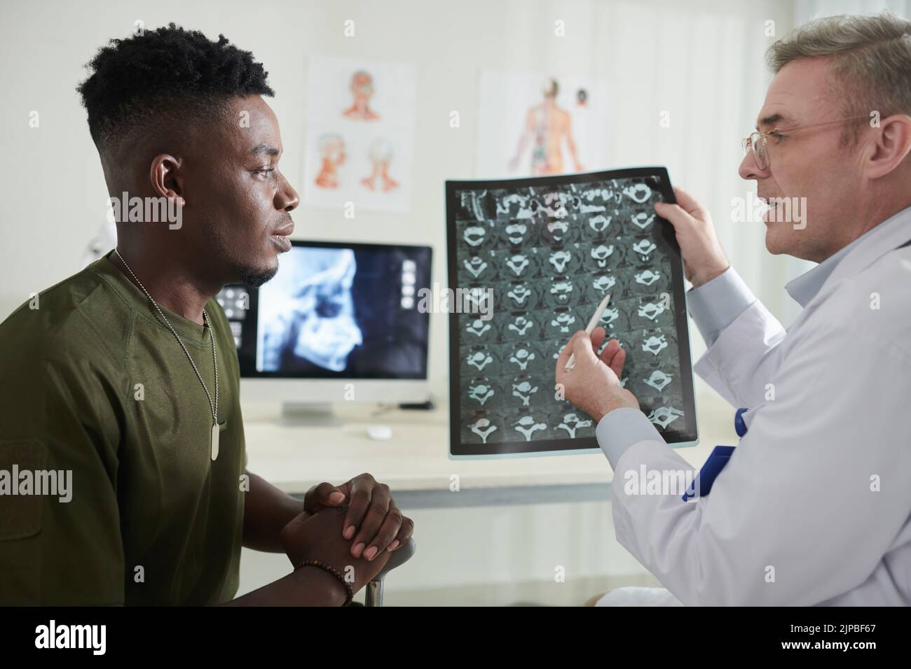 Serious doctor pointing at MRI image of spine when talking to military ...