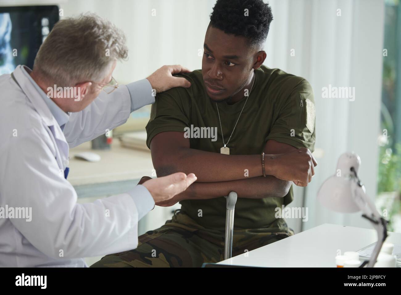 Young Black soldier with cane listening to supportive doctor giving ...