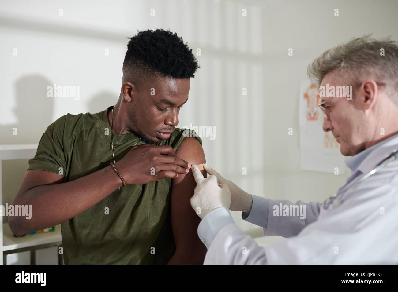 Doctor sticking adhesive bandage on vaccine injection site on arm of ...