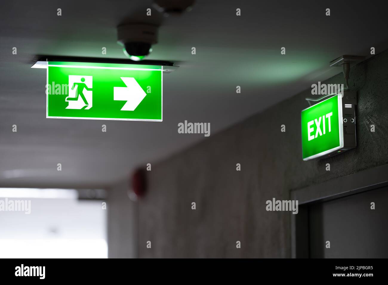 A green fire exit sign is placed on the ceiling along the dimly lit ...