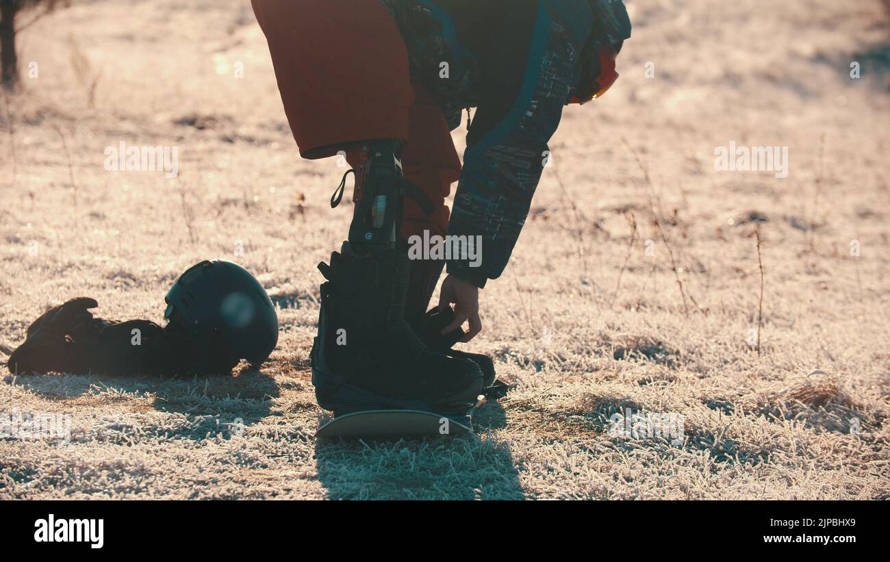 A man with prosthetic leg standing on the board and setting boots on it ...