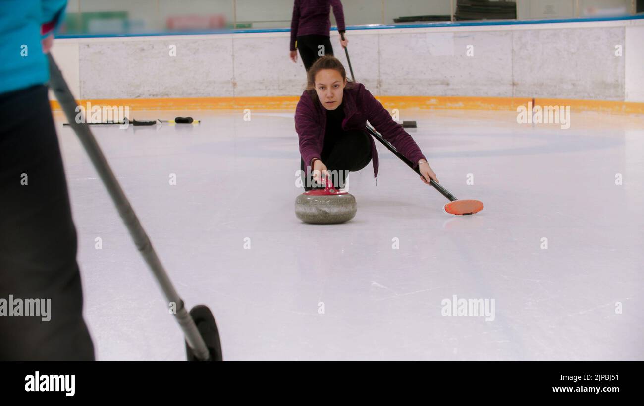 Curling - a young woman pushes off in the ice field with a granite ...