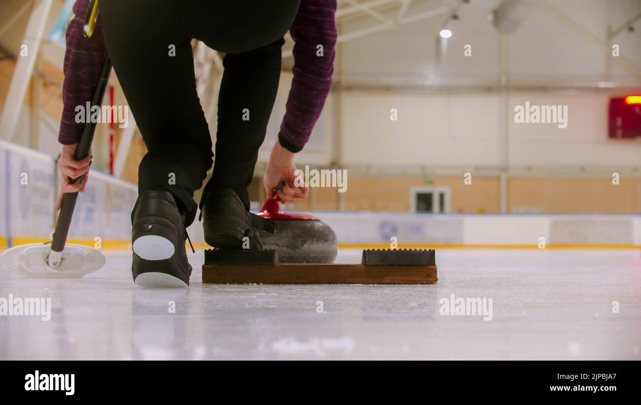 Curling training - a woman about to push off the stand on the ice field ...