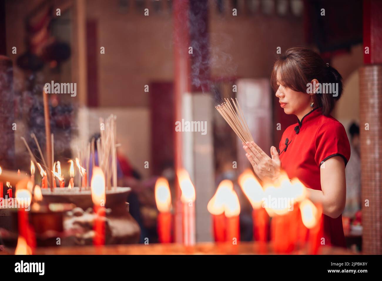 An Asian woman lighting incense sticks to pay homage to the Chinese New ...
