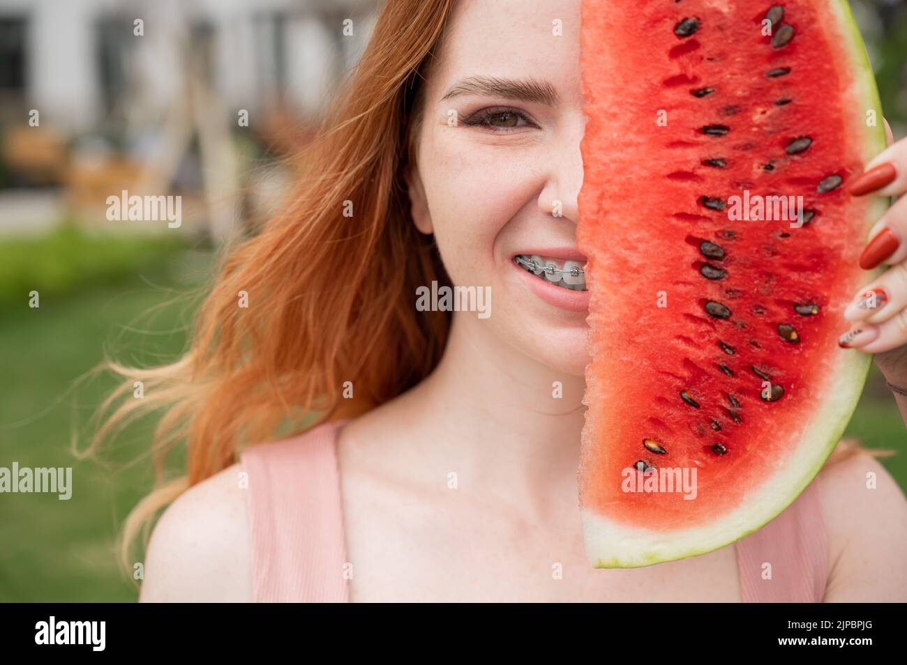 Beautiful red-haired woman smiling with braces on her teeth covers half ...