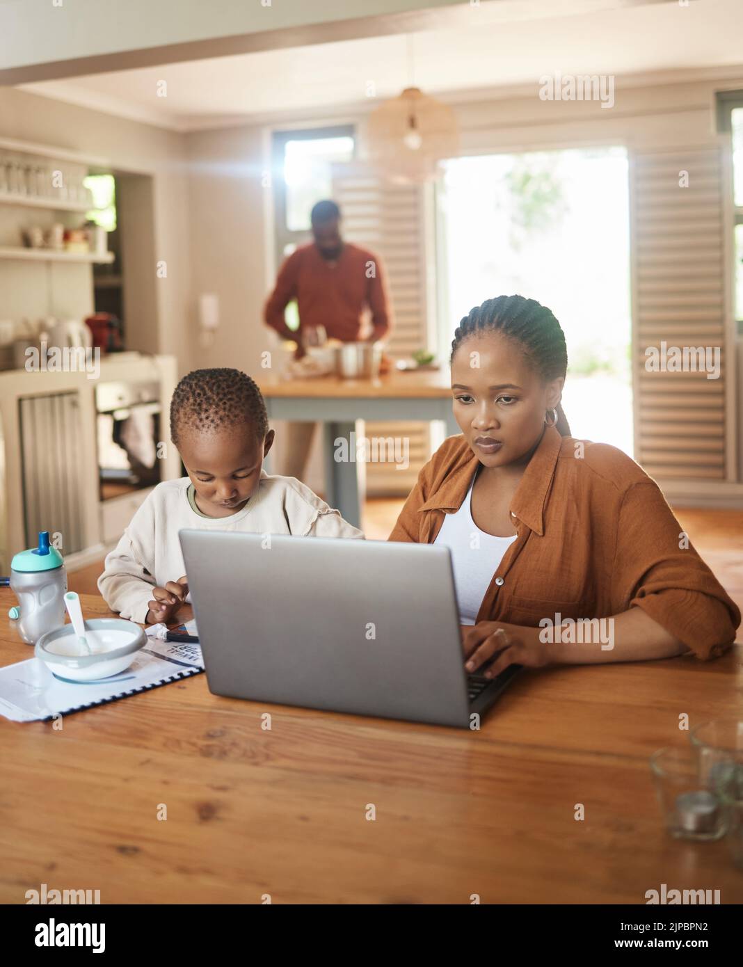Busy, serious and multitask mother working on laptop while taking care ...