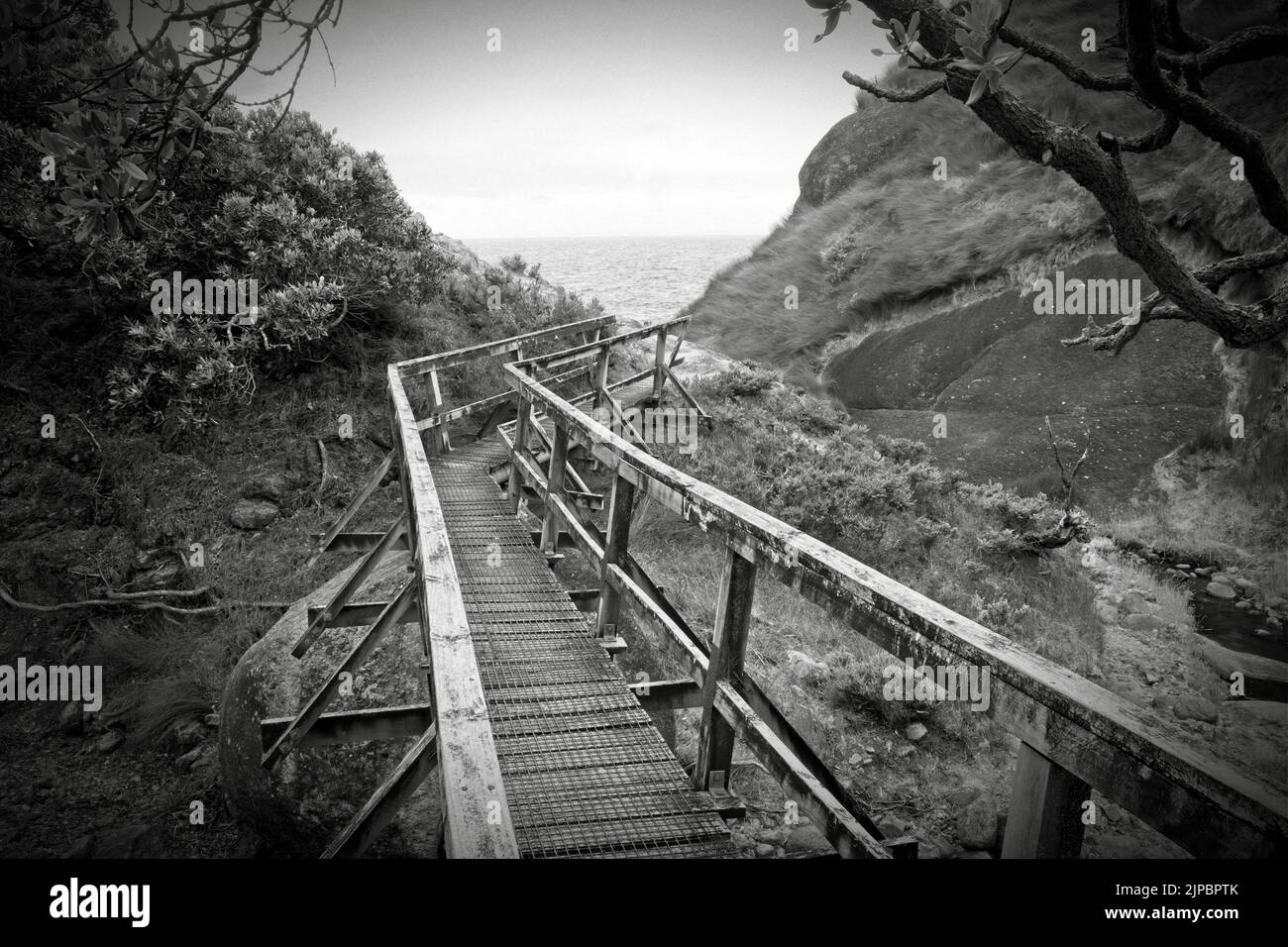 Walkway Bridge, balanced on a rock, towards the ocean in black and ...