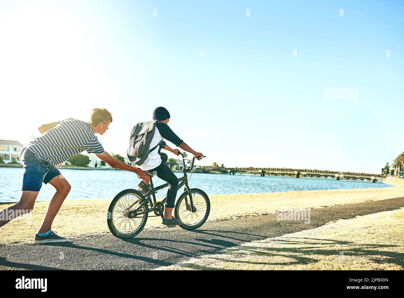 Giving him a push. a young boy teaching his younger brother how to ride ...
