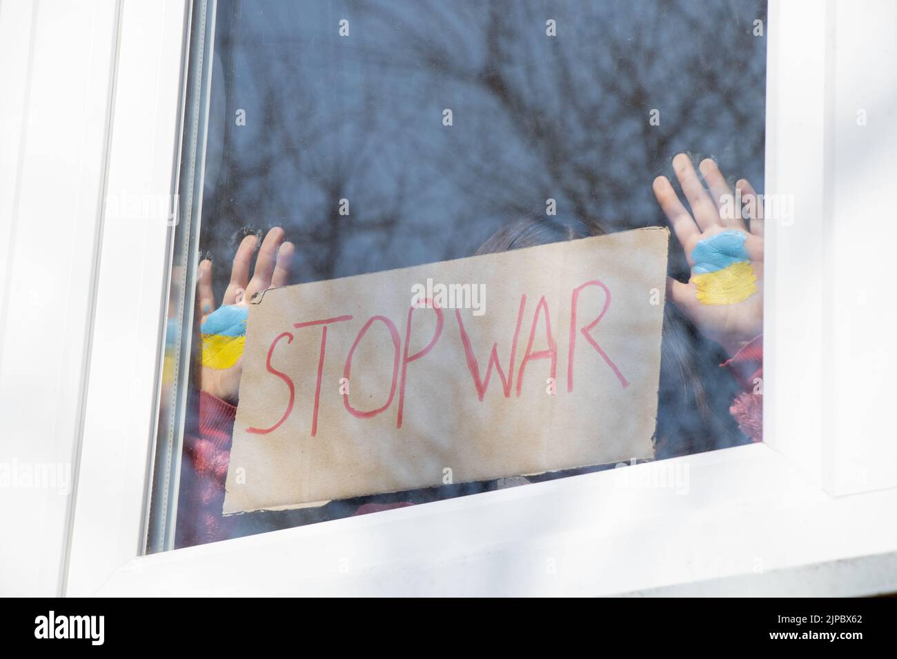 A little girl in the window of her house holds a poster stop war and ...