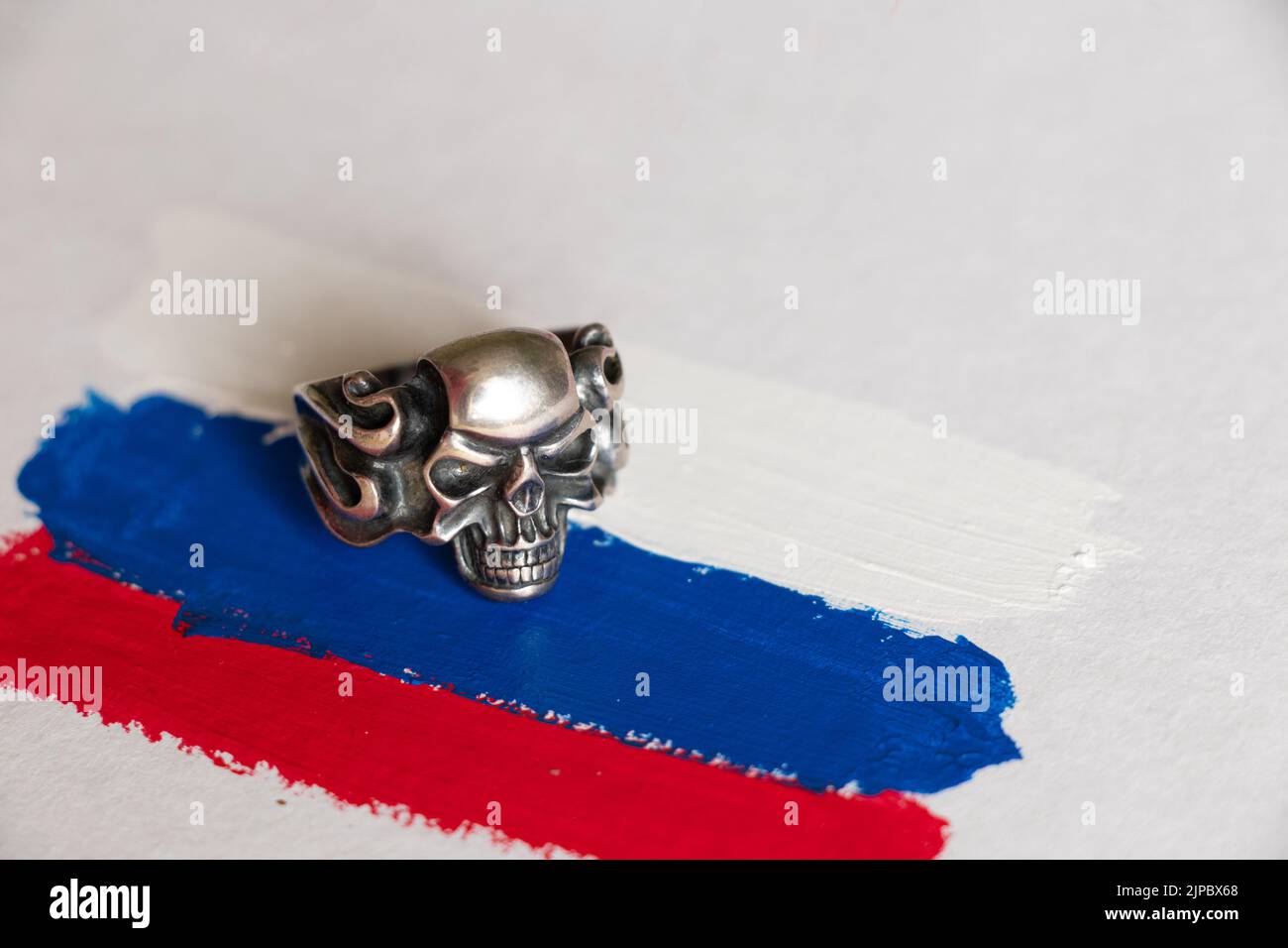 A silver ring with a skull lies on a painted Russian flag on white ...