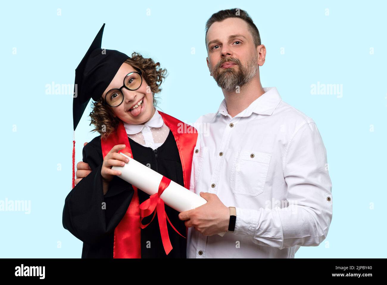Joyful female child in graduation cap and ceremony robe holds ...