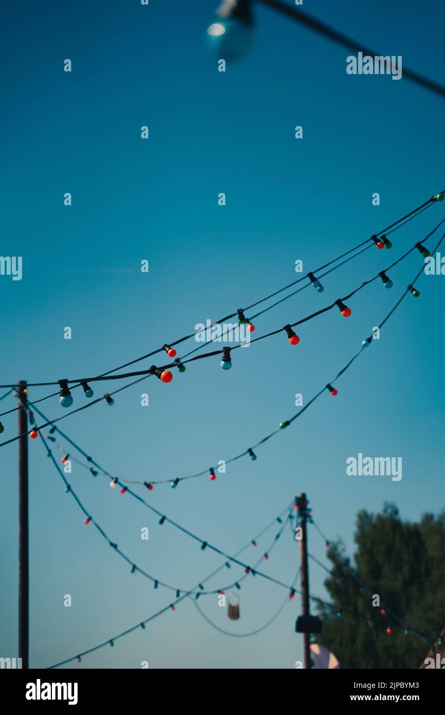 A vertical shot of a light garland hanging on a blue sky background ...